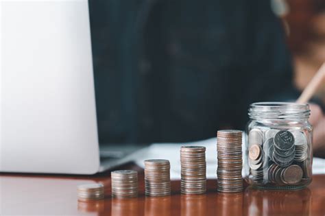보고서가 있는 노트북 쌓인 동전 책상 위의 유리 돼지 저금통을 들고 일하는 사업가 저축 돈 은행 예금 이자 징수 및 세금 개념 사업 성장 재무 관리의 상승 추세 개념에 대한