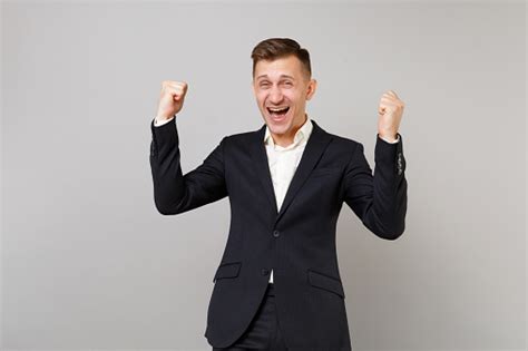 고전적인 검은 양복 스튜디오에서 회색 벽 배경에 고립 된 승자 제스처를 하 고 셔츠에 젊은 비즈니스 남자를 웃 고의 초상화 업적 경력 자산 사업 개념 복사 공간을 모의