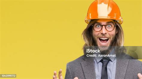 안전을 입고 긴 머리를 가진 젊은 잘생긴 Architec 남자 미친을 축 하 하는 고립 된 배경 위에 헬멧 하 고 무기와 성공을 위한 흥분 비명 제기 및 오픈 눈 깜짝