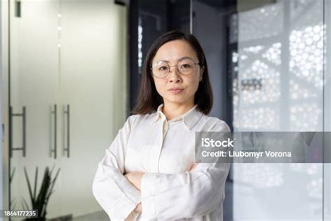 성숙한 경험 많은 아시아 여성 사업가 상사 진지하게 카메라를 바라보는 여성 노동자 성공적인 성취를 확신하는 사무실 건물 안에서 팔짱을 끼고 안경을 쓴 여성의 초상화 30