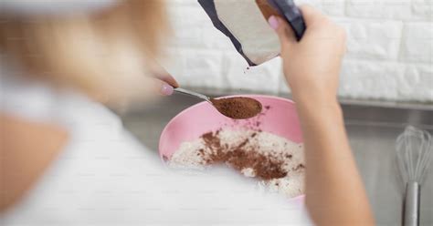 제과 개념입니다 아몬드 가루와 함께 분홍색 그릇에 카카오 가루를 넣고 여성 페이스트리 셰프의 전문 손의 뒷모습을 닫습니다 카카오와 함께 찻 숟가락에 집중하십시오 사진