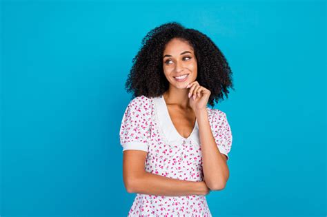 꽃무늬 드레스를 입은 장난기 많은 젊은 여성이 생생한 파란색 배경을 배경으로 따뜻하게 미소 지으며 자연스러운 우아함과 기쁨을