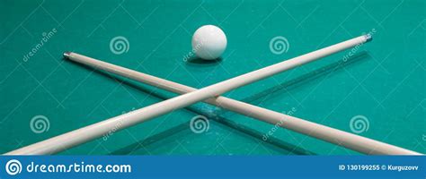 Two Pool Cues Crossed In Front Of A White Ball On A Green Table Stock
