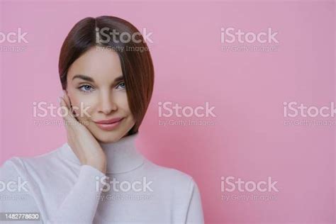 유쾌한 어두운 머리의 젊은 여성의 고립 된 샷은 잘 손질 얼굴을 가지고 터틀 넥 점퍼를 입고 건강한 피부를 가지고 장밋빛 배경에 고립 사람 아름다움 웰빙 컨셉 깔끔한에 대한