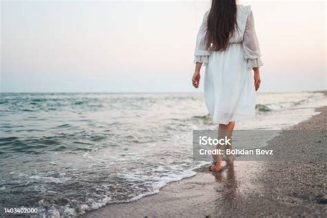 긴 머리와 모자를 쓴 긴 흰색 드레스를 입은 아름다운 젊은 여성이 해변을 따라 간다 여자에 대한 스톡 사진 및 기타 이미지 여자 한 명의 여자만 드레스 Istock
