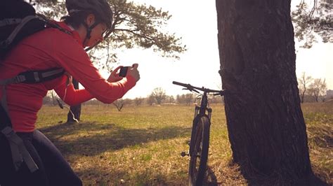 젊은 백인 여성 운동 선수 관광 자전거는 전화로 사진을 찍고 화창한 날에 나무 근처에 서있는 자전거를 촬영합니다 헬멧과 스포츠