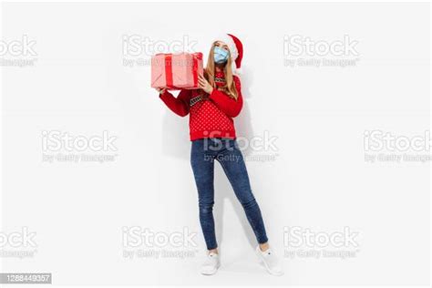 전체 길이 겨울 크리스마스 스웨터 산타 클로스 모자와 그녀의 얼굴에 의료 마스크 흰색 배경 위에 선물 상자를 들고있는 동안 재미 12월에 대한 스톡 사진 및 기타 이미지