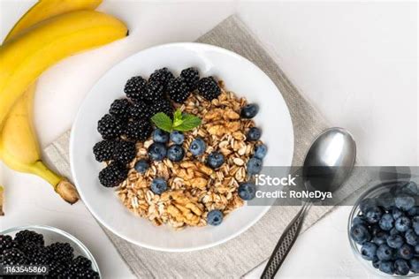 건강한 아침 식사 홈메이드 그래놀라 뮤즐리 블랙베리 블루베리 견과류 꿀 민트가 있는 시리얼을 흰색 바탕에 흰색 그릇에 담았습니다 0명에 대한 스톡 사진 및 기타 이미지