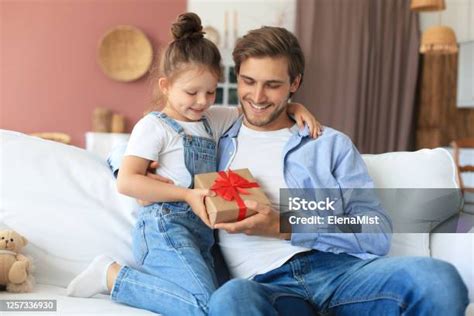 귀여운 아이 딸은 아빠에게 놀라움을 선사하고 어린 소녀는 소파에 앉아 아버지에게 선물 상자를 선물합니다 아버지의 날 딸에 대한 스톡 사진 및 기타 이미지 Istock