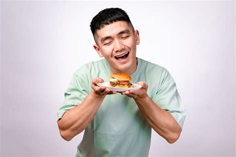 민트 그린 셔츠를 입은 동양인 남성이 눈을 감고 하얀 접시에 담긴 치즈버거를 들고 그 향기를 즐기는 듯 보인다 배경은 일반 흰색입니다 30 34세에 대한 스톡 사진 및 기타