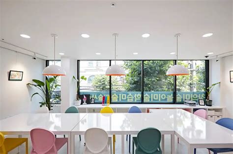 팬던트 조명과 화이트톤의 넓은 테이블 다채로운 색상의 캐주얼 의자가 돋보이는 미술 교습소 실내 사진