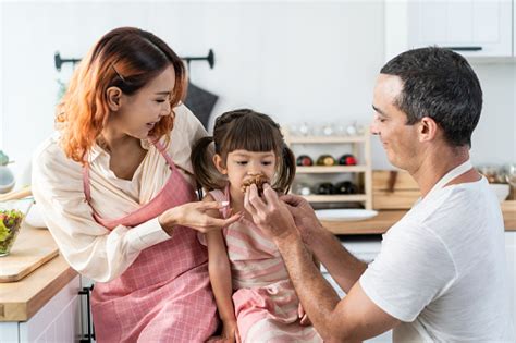 아시아 의 매력적인 부모는 부엌에서 귀여운 아기 딸에게 컵 케이크를 공급합니다 행복한 가족 사랑하는 커플 베이킹 및 집에서 점심