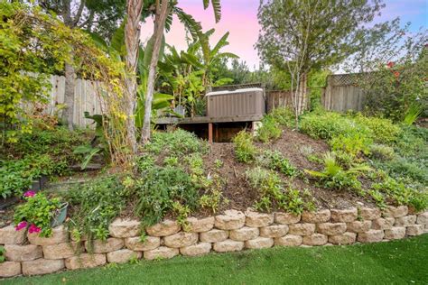 Stone Wall With Shrubs And Trees Adjacent To A Fenced In Backyard Stock
