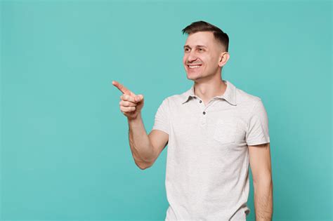 캐 쥬얼에 서 있는 젊은 남자의 초상화는 스튜디오에서 파란색 청록색 배경 옆에 고립 된 포인팅 검지 손가락 사람들은 진심으로 감정 라이프 스타일 개념입니다 복사 공간을 모의