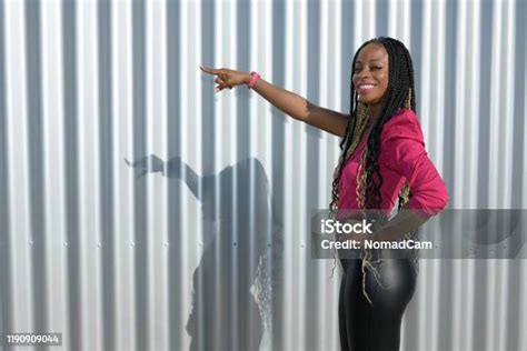 긴 검은 색과 금발 머리띠가 왼쪽을 가리키고 배경에 금속 울타리가있는 카메라를 바라보는 동안 미소를 짓는 아프로 스타일의 흑인 소녀 땋은 머리에 대한 스톡 사진 및 기타