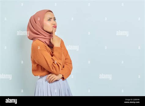 Pensive Young Asian Muslim Woman In Brown Sweater And Hijab Looking Serious Thinking About A