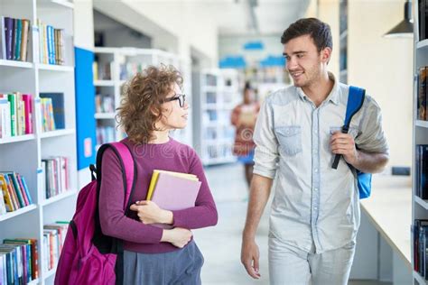 Весёлые студенты обсуждая книгу в библиотеке Стоковое Изображение изображение насчитывающей