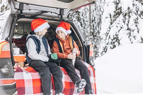 크리스마스를 위해 장식 된 자동차 트렁크에 보온병이있는 빨간 산타 모자를 쓴 두 친구 십대 소년 도로 여행 모험과 지역 여행 개념 눈 덮인 숲에서 겨울 피크닉 새해 휴가