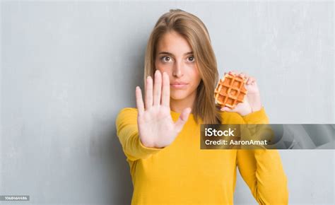 심각 하 고 자신감 표현 방어 제스처 정지 표시를 하 고 오픈 손으로 와플을 먹는 그런 지 회색 벽에 아름 다운 젊은 여자 경계