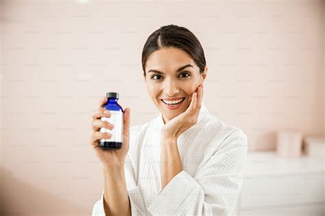 분홍색 배경에 격리된 건강과 관리를 위한 치료제 병을 들고 목욕 가운을 입은 쾌활한 아름다운 아가씨의 초상화 사진 Unsplash의 건강한 라이프 스타일 이미지