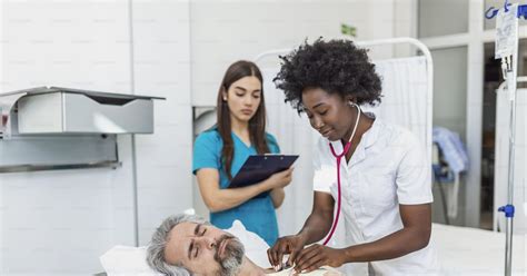 아프리카 계 미국인 여성 의사와 함께 아픈 남자 환자는 병원 응급실에서 청진기로 가슴을 듣습니다 의사와 간호사가 병실에서 노인