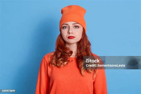 모자를 쓴 심술궂은 무디소녀의 초상화와 파란 배경위에 고립된 카메라를 바라보는 따뜻한 점퍼 곱슬머리와 빨간 입술을 가진 여성 기분을 상하게 하는 여성 슬프고 화가 난다 20