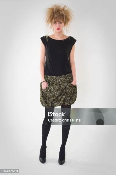 흰색 바탕에 카메라를 보고 미친 머리 스타일과 어두운 셔츠와 치마에 포즈 여자의 전체 길이 초상화 패션 스튜디오 촬영 곱슬