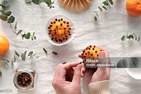 귤과 정향으로 손으로 만든 라그랑트 포맨더 볼을 들고 있는 손 향기로운 겨울 녹색 유칼립투스가 있는 흰색 섬유 식탁보에 평평하게 누워 있습니다 12월에 대한 스톡 사진 및