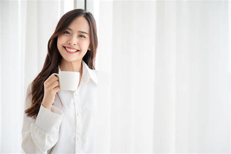 젊은 아시아 아름 다운 여자 의류 흰색 잠옷과 침실에서 아침에 창 옆에 커피를 마십니다 그녀는 행복한 신선한 느낌과 미소 휴식 마시기에 대한 스톡 사진 및 기타 이미지