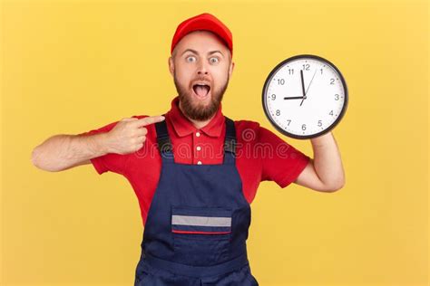 Surprised Man Worker Pointing At Big Wall Clock In His Hands Looking At Camera With Open Mouth