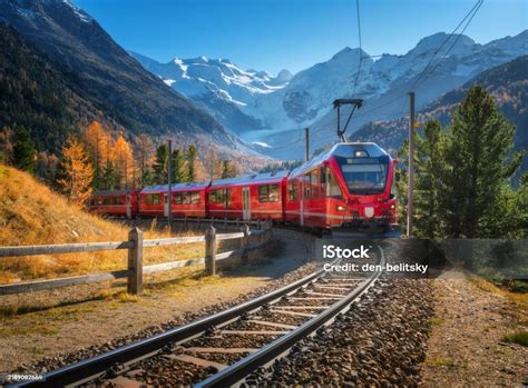 스위스의 눈 덮인 봉우리와 활기찬 가을 나무가 있는 멋진 높은 산을 통과하는 철도를 따라 여행하는 빨간색 현대식 전기 열차