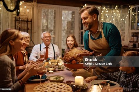 식탁에서 그의 대가족에게 추수 감사절 칠면조를 제공하는 행복한 아버지 추수감사절에 대한 스톡 사진 및 기타 이미지 추수감사절 가족 저녁 식사 Istock