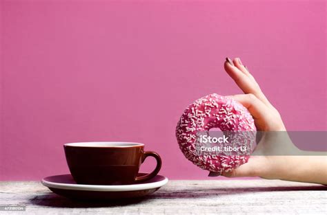 손을 들고 나무 테이블에 분홍색 배경에 뿌리와 다채로운 도넛 커피 한잔입니다 도넛의 두 종류입니다 케이크와 달콤한 음식 세부입니다 닫습니다 파스텔 컬러 건강관리와 의술에