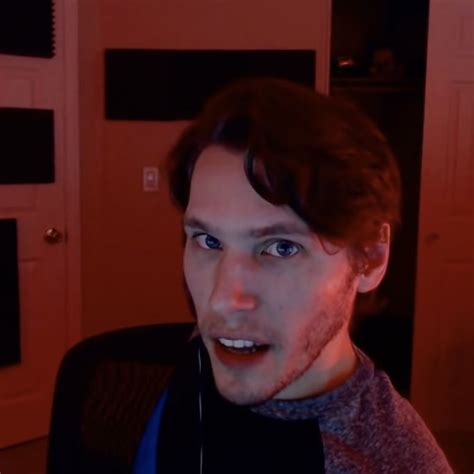 A Babe Man With Dark Hair And Blue Eyes Is Looking At The Camera While Sitting In Front Of An