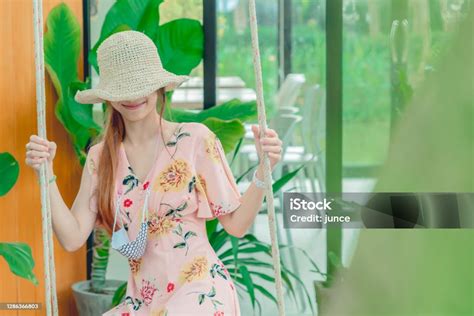 여름 모자를 쓴 아시아 계 중국인 여성이 집 정원에서 그네에 앉아 있다 25 29세에 대한 스톡 사진 및 기타 이미지 25 29세 나무 낮 Istock