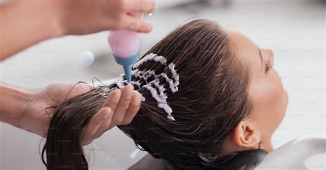 아름다운 여자가 미용실에서 머리를 감고 있다 그녀는 기쁨과 휴식으로 앉아 있습니다 미용사가 샴푸 한 병을 들고 고객의