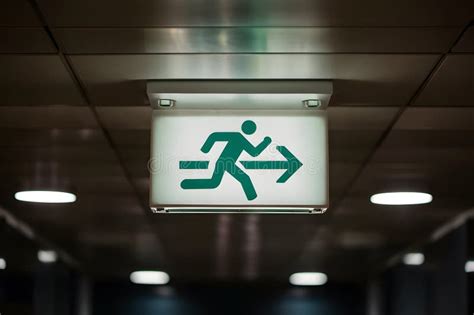 Glowing Emergency Exit Sign With Running Figure And Arrow In Dim Lighting Stock Photo Image Of