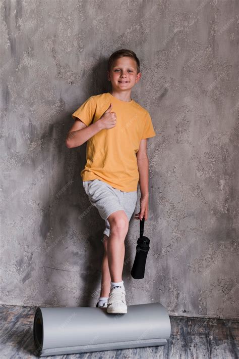 Улыбающийся мальчик стоя перед бетонной стеной показывает палец вверх Бесплатно Фото