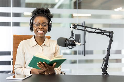 현대 녹음 스튜디오에서 웃는 여자가 헤드폰을 착용하고 마이크 앞에서 책을 읽고 있습니다 그녀는 팟캐스트를 진행하고 창의적인 환경에서 청중과 소통할 준비가 되어 있습니다