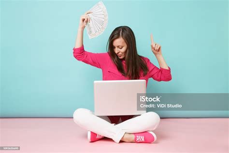 전체 길이 장미 셔츠 블라우스에 젊은 여자의 초상화 바닥에 앉아 흰 바지 핑크 블루 파스텔 벽 배경 스튜디오에 고립 된 돈을