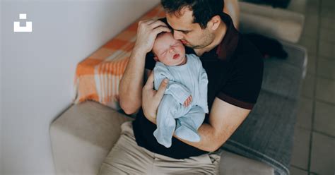 검은 색 크루 넥 티셔츠를 입은 남자는 파란색과 흰색 줄무늬 Onesie에서 아기를 안고 있습니다 사진 Unsplash의