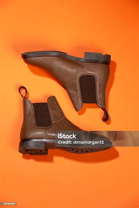 신발 개념 클래식 브라운 샤그린 가죽 Chealsea 부츠 한 켤레의 플랫레이 이미지로 오렌지 배경 위에 서로 가까이 배치된