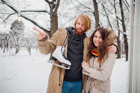 겨울 그리고 날짜입니다 겨울 눈 덮힌 나무 공원에서의 배경에서 여자와 남자와 사랑에 젊은 부부는 포옹 긴 머리와 수염 남자 스케이트를 유지 하 고 여자 친구를 사랑 12월에