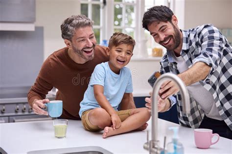 Same Sex Family With Two Dads Taking Selfie In Kitchen With Son Sitting On Counter Stock Photo