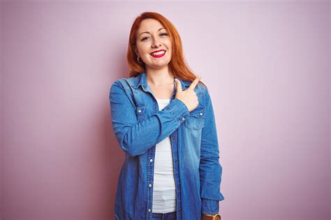 Youg 아름다운 빨간 머리 여자는 고립 된 분홍색 배경 에 서 데님 셔츠를 입고 얼굴에 행복하고 자연스러운 표정으로 손과