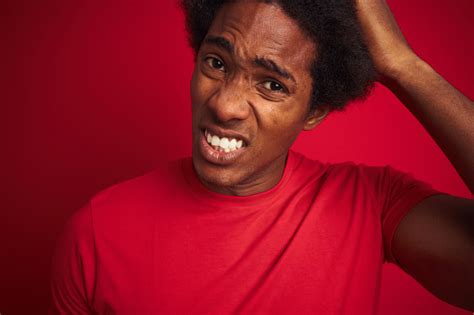 고립된 빨간 배경 위에 서있는 티셔츠를 입은 젊은 미국 남자는 머리에 손으로 스트레스를 받고 수치심과 깜짝 얼굴에 충격을 받았으며 화가 나고 좌절했습니다 실수에 대한