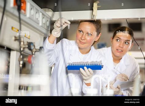 Serious Female Chemists Making Report Examining Solution In Test Tube For Reaction In Research