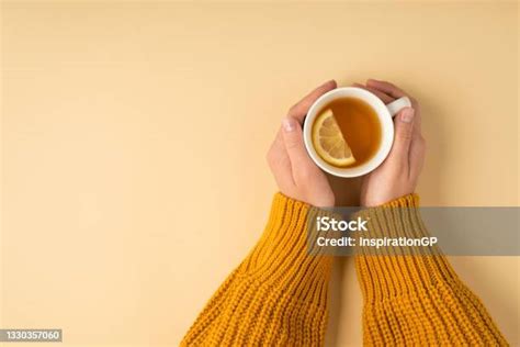 카피 스페이스와 고립 된 파스텔 오렌지 배경에 레몬 슬라이스와 차의 흰색 컵을 들고 노란색 스웨터에 여성의 손의 1 인칭 최고