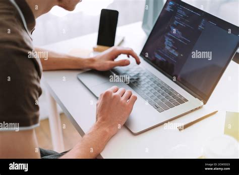 Young Man Mobile Developer Programmer Writes Program Code On A Laptop