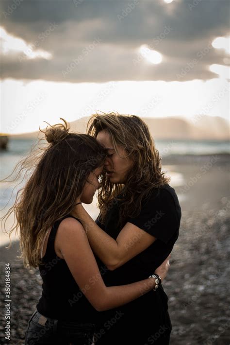 Pareja de dos chicas morenas jóvenes que son novias lesbianas besándose en la playa junto al mar